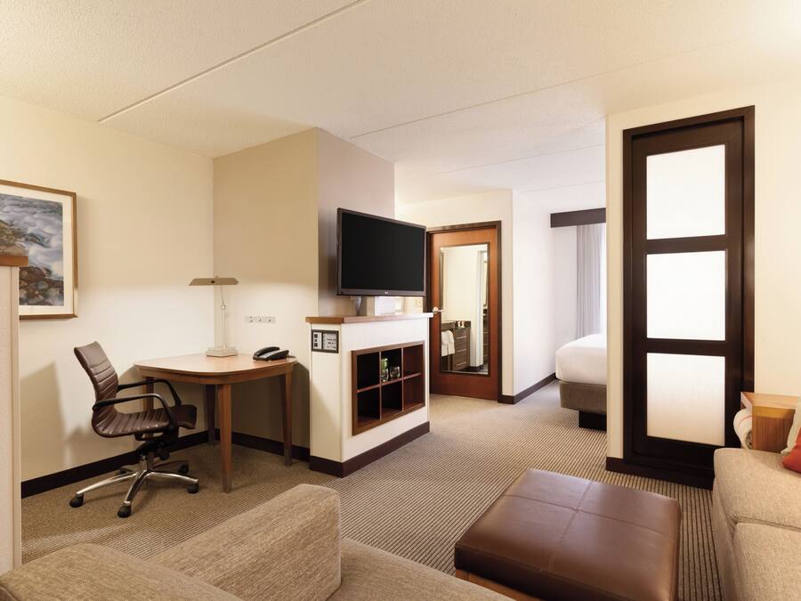 Quarto de hotel com escrivaninha, cadeira, televisão, sofá e apoio para os pés.