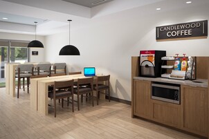 Interior moderno de café com mesa e cadeiras de madeira, um laptop sobre a mesa, uma máquina de café e uma placa com a inscrição "CANDLEWOOD COFFEE".