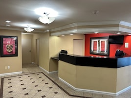 Uma área de recepção de hotel, com balcão, placa de boas-vindas emoldurada e uma porta.