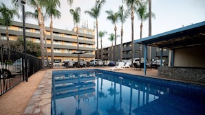 Piscina com espreguiçadeiras, palmeiras e um edifício de vários andares ao fundo.