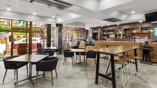 Interior moderno de café com mesas, cadeiras, balcão e amplas janelas.