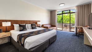 Quarto de hotel com cama grande, uma mesa, uma cadeira e vista para o verde lá fora.