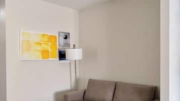 Uma sala de estar moderna com um sofá cinza, um banquinho amarelo e uma luminária fixada na parede.