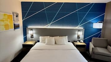 Quarto de hotel com uma cama grande, duas mesas de cabeceira com abajures, uma cadeira e parede com padrão geométrico.