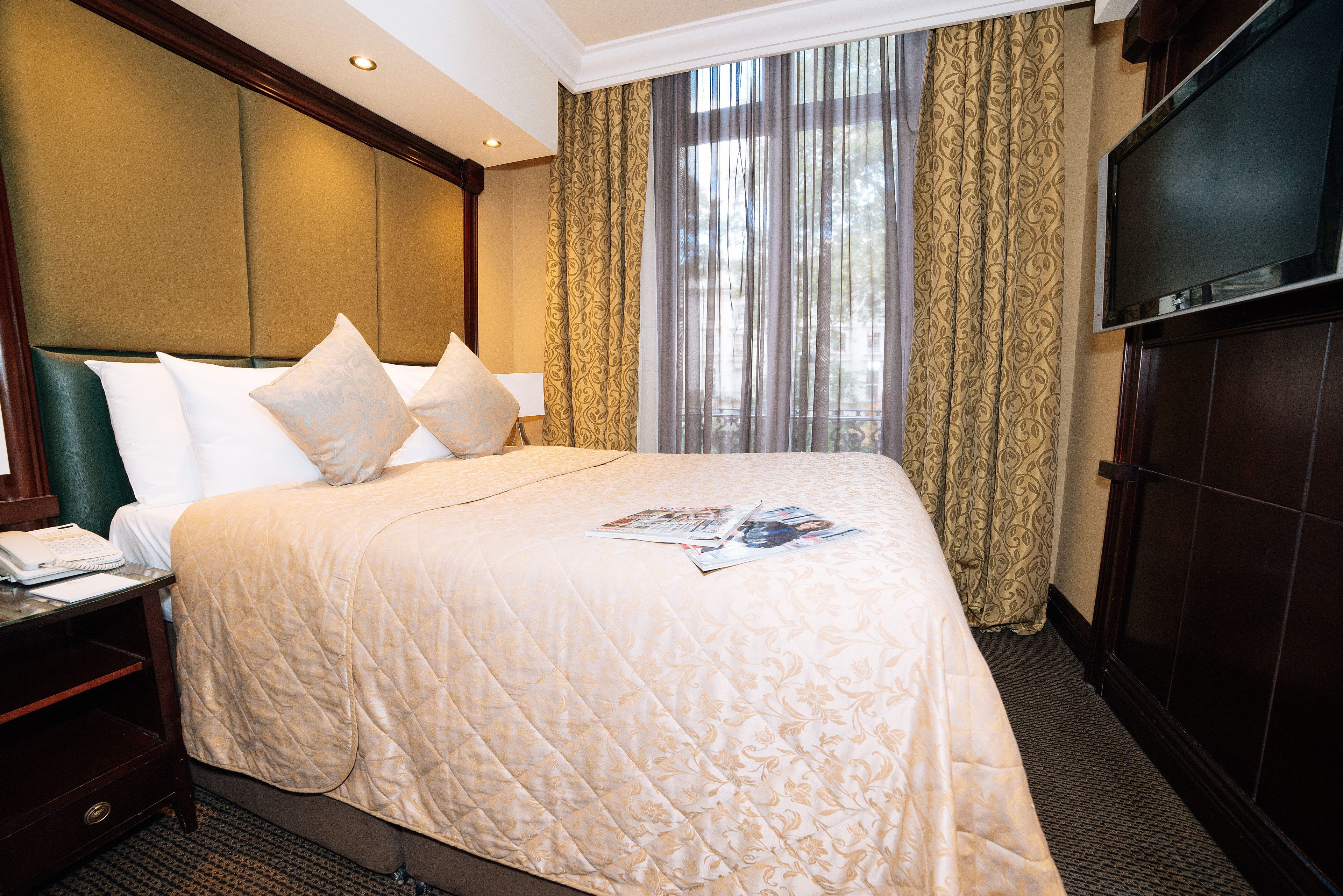 Quarto de hotel com uma cama grande, televisão de tela plana e janela com cortinas estampadas.