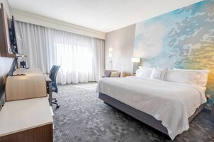 Quarto de hotel com uma cama grande, uma escrivaninha com computador, uma cadeira e uma televisão.
