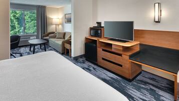 Quarto de hotel com uma cama grande, televisão, micro-ondas, escrivaninha e uma cadeira.