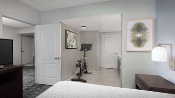 Quarto de hotel com cama, escrivaninha, televisão e bicicleta de exercício, com obras de arte nas paredes.