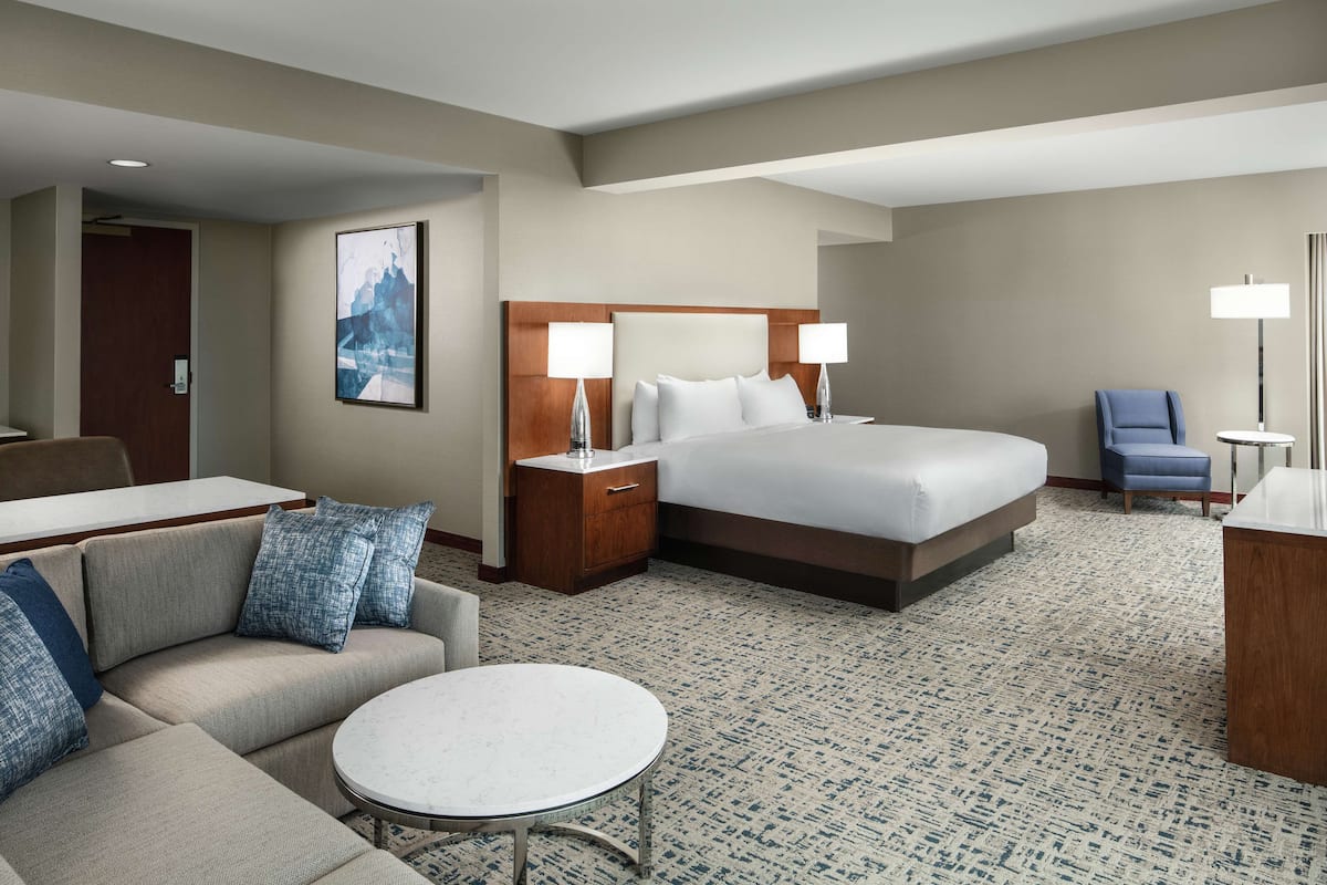 Quarto de hotel com uma cama grande, um sofá, uma mesa redonda e uma escrivaninha.