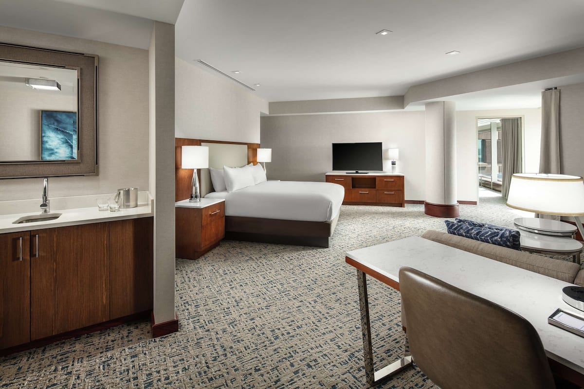 Quarto de hotel com cama, escrivaninha, televisão e banheiro.