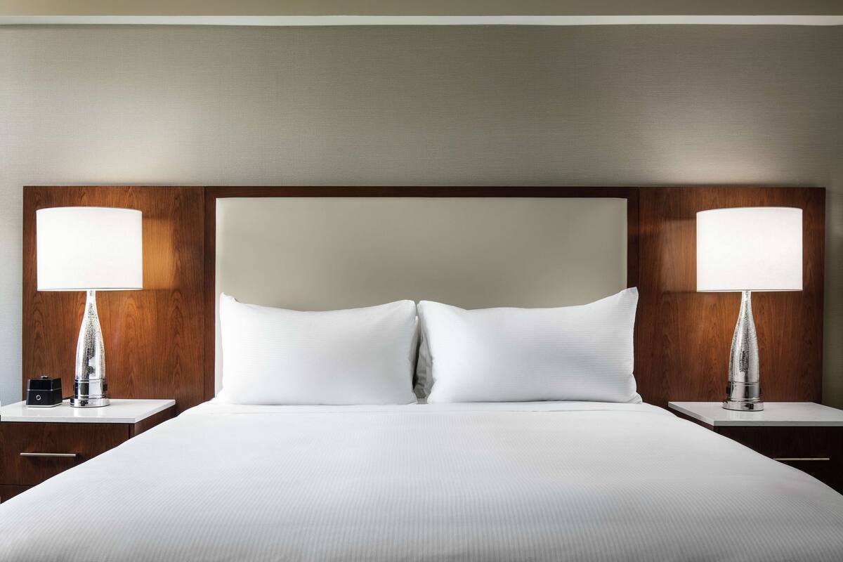Quarto de hotel com uma cama grande, duas mesas de cabeceira e duas luminárias.