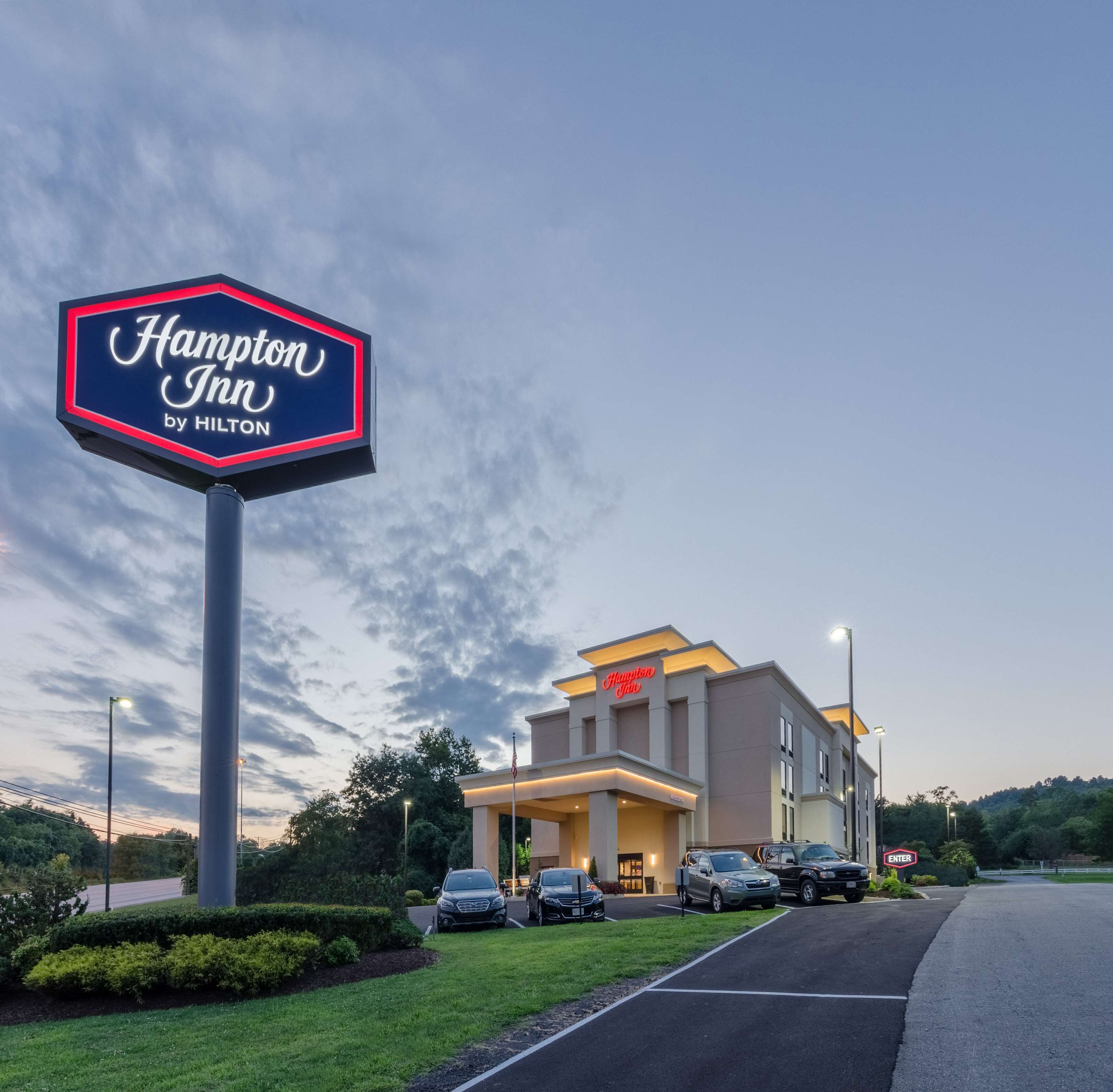Um hotel Hampton Inn by Hilton com uma placa grande, um estacionamento com vários carros e um gramado bem cuidado.
