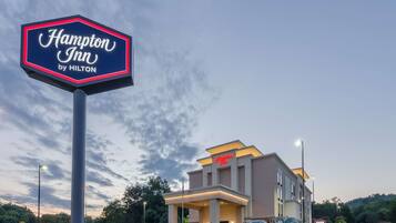 Um hotel Hampton Inn by Hilton com uma placa grande, um estacionamento com vários carros e um gramado bem cuidado.