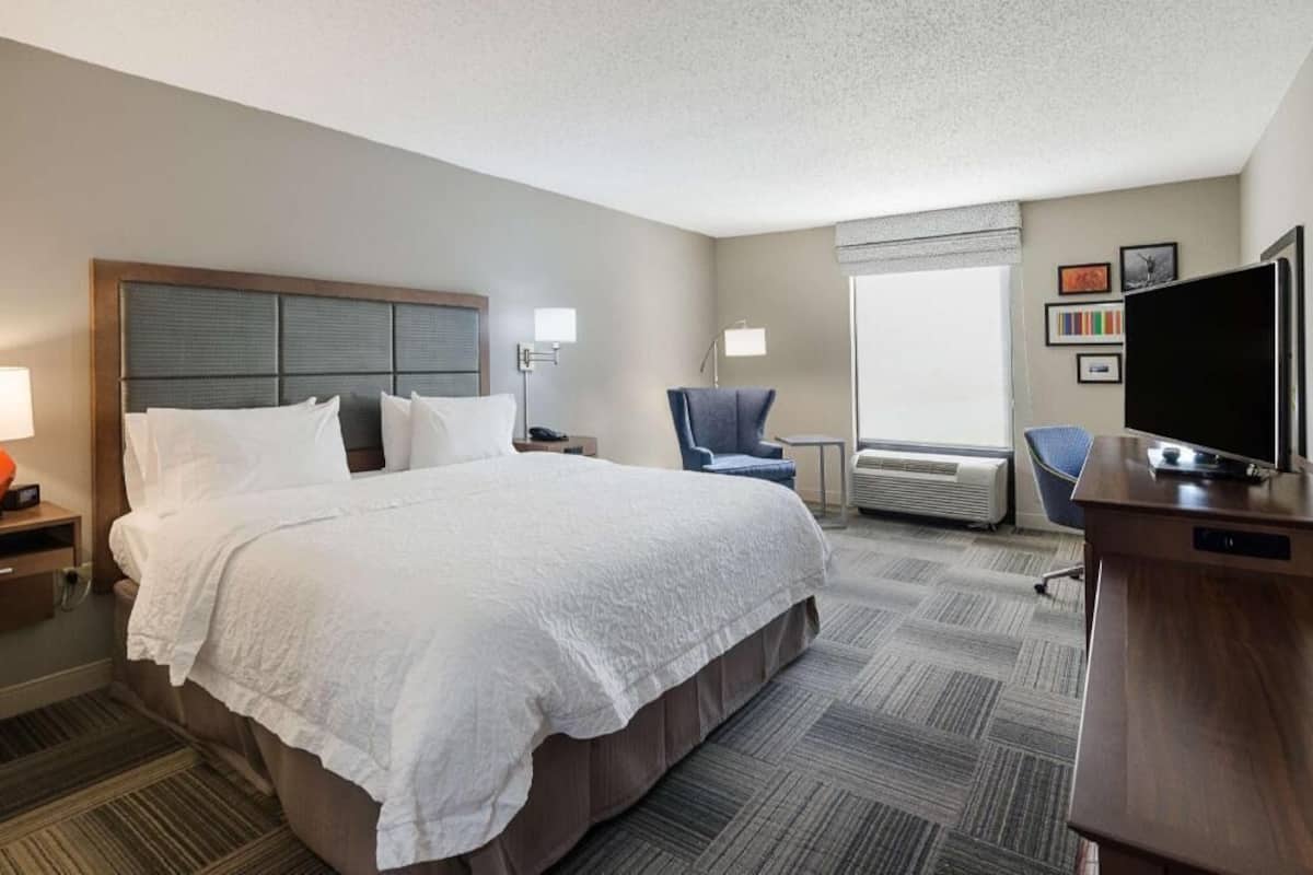 Quarto de hotel com cama, escrivaninha, cadeira, ar condicionado e televisão.