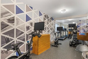 Academia com bicicletas ergométricas, esteiras e parede de painel de madeira.