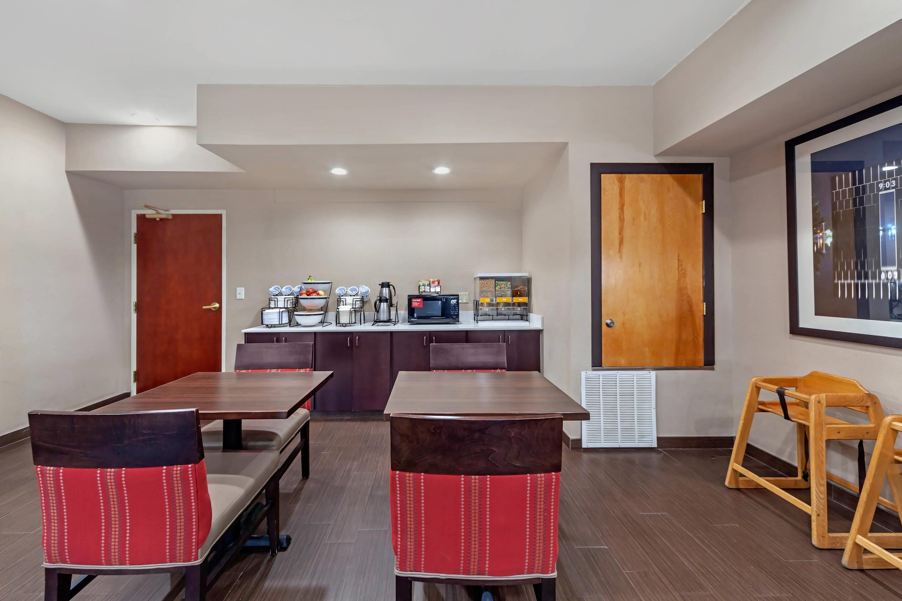 Uma sala de jantar com uma mesa comprida e cadeiras, uma cozinha ao fundo e um quadro pendurado na parede.