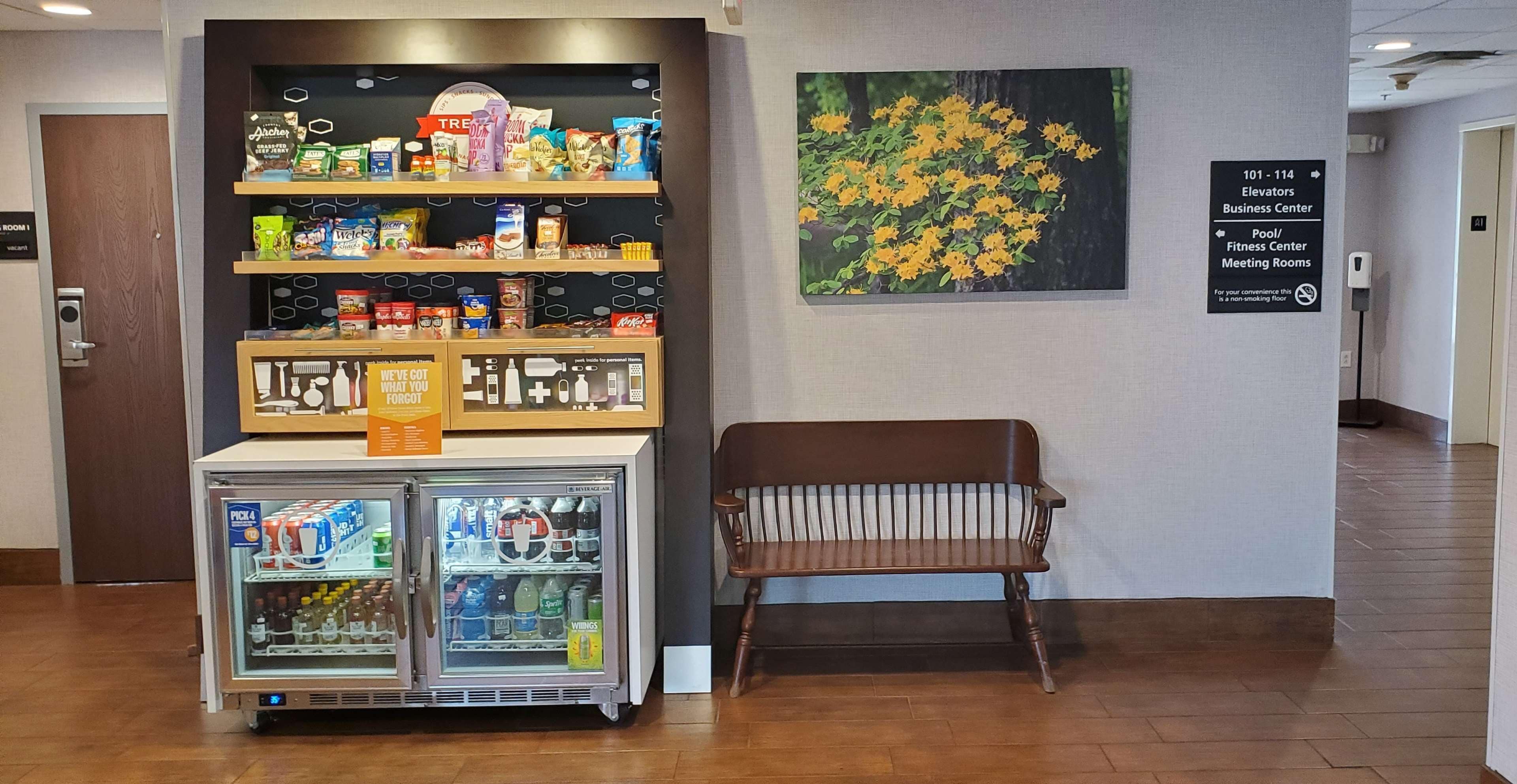 Máquina de vendas com lanches e bebidas, um banco e um aviso na parede indicando elevadores e salas de reunião.