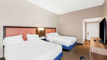 Quarto de hotel com duas camas, uma mesa, uma televisão e uma porta.