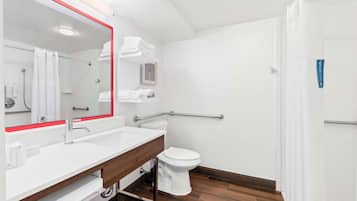 Casa de banho moderna com lavatório branco, espelho e sanita. Toalhas empilhadas numa prateleira e zona de duche com porta de vidro.