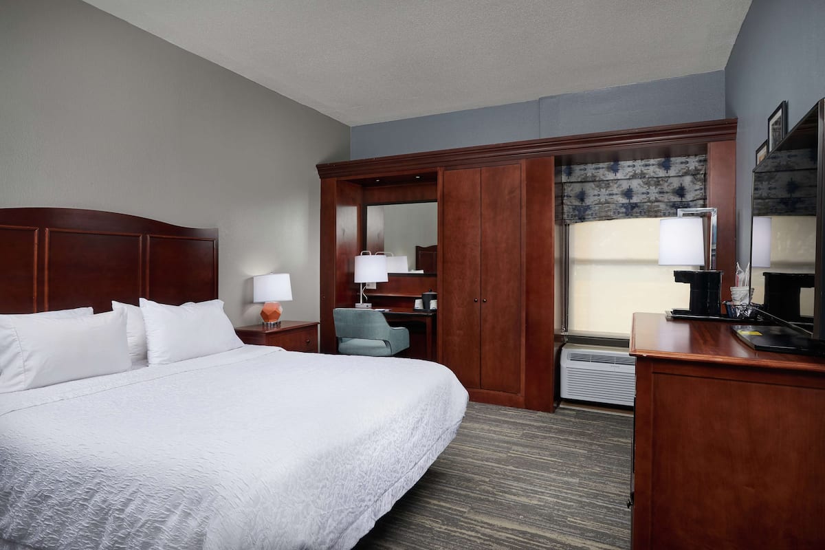 Quarto de hotel com uma cama grande, uma escrivaninha, uma cadeira e um guarda-roupa.