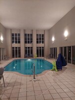 Piscina interior com água cristalina, rodeada por pavimento cerâmico e um aviso de 'Não Mergulhar'.