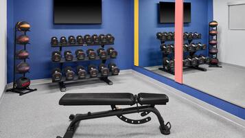 Uma academia com um banco, halteres e bolas de exercício.