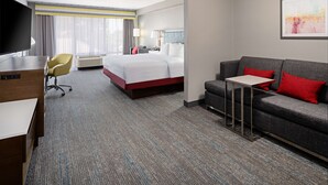 Quarto de hotel com cama, sofá, escrivaninha, televisão e janela com cortinas.