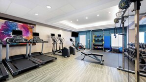 Uma academia com esteiras, elípticos, um banco e equipamentos de musculação.