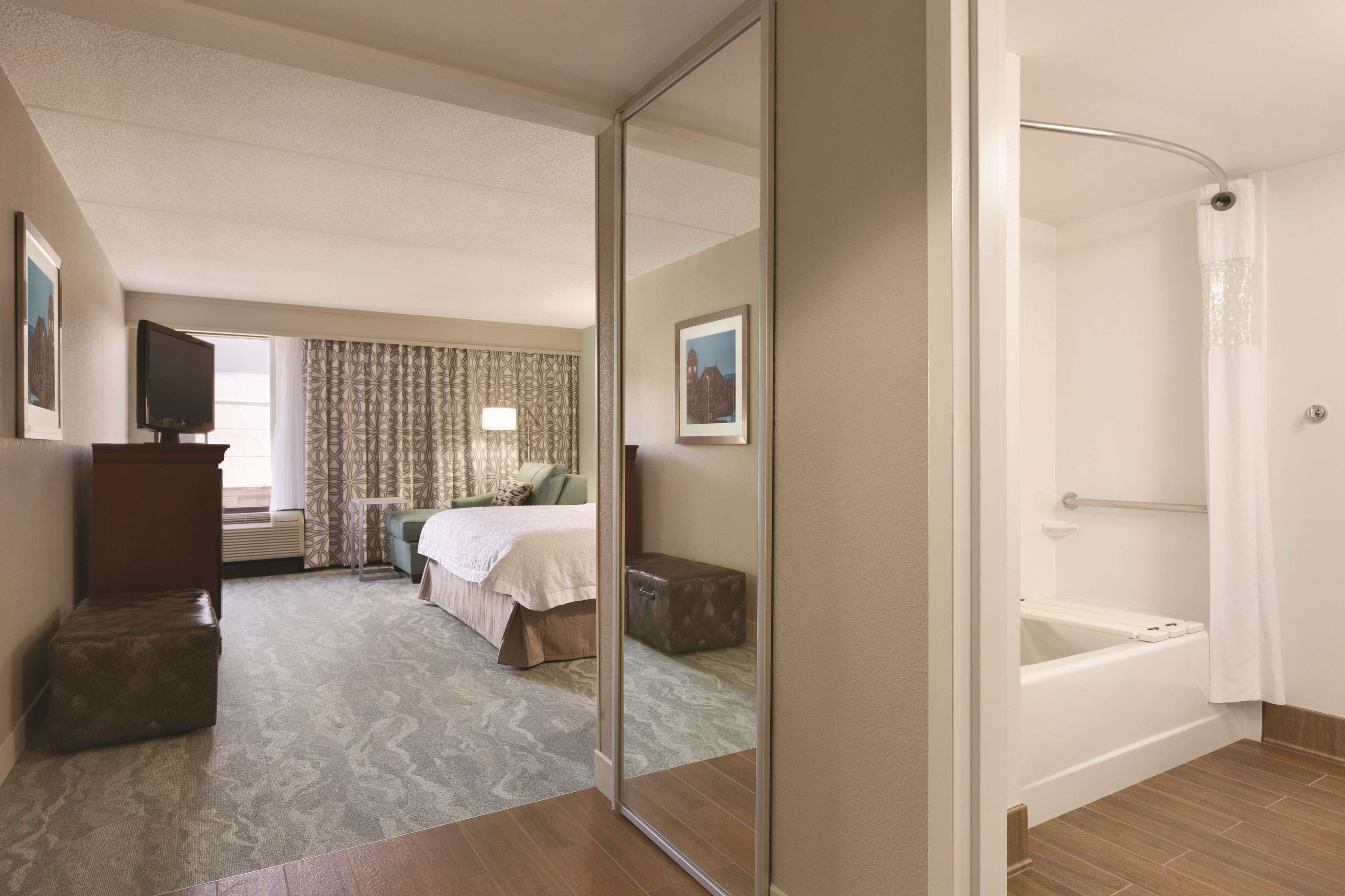Quarto de hotel com cama, televisão, banheiro com banheira e um espelho grande.