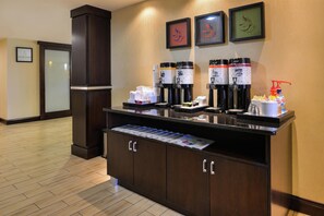 Uma área de recepção de hotel com um canto de café, obras de arte emolduradas na parede e um suporte para revistas.