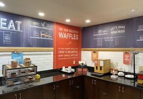 Balcão de pastelaria com um letreiro a promover waffles, uma máquina de café e diversos produtos de pastelaria.