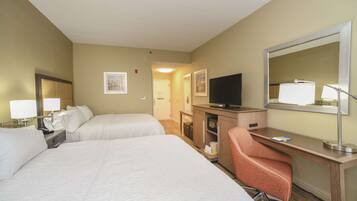 Quarto de hotel com duas camas, uma escrivaninha, uma cadeira, uma televisão e um espelho.