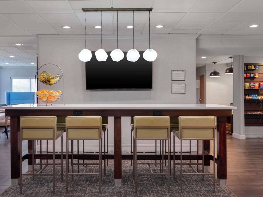 Uma área de bar moderna com uma TV de tela plana, luminárias pendentes e banquetas.