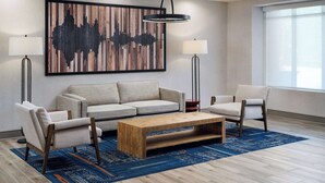 Uma sala de estar moderna com um sofá, duas poltronas, uma mesa de centro e um grande quadro abstrato na parede.