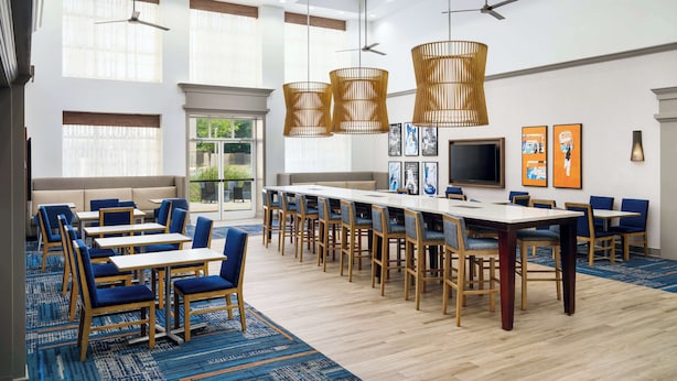 Uma sala de jantar ampla com pé direito alto, grandes janelas e luminárias modernas.
