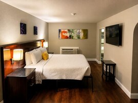 Quarto de hotel com cama, abajures, televisão de tela plana, quadro na parede e aquecedor.