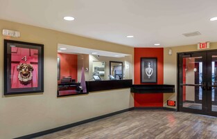 Um saguão de hotel com uma mesa de recepção, um espelho e uma porta de saída.