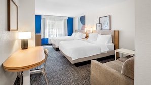 Quarto de hotel com duas camas, uma escrivaninha, uma cadeira e uma pequena mesa.