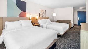 Quarto de hotel com duas camas, uma escrivaninha, uma cadeira, um abajur e obras de arte na parede.
