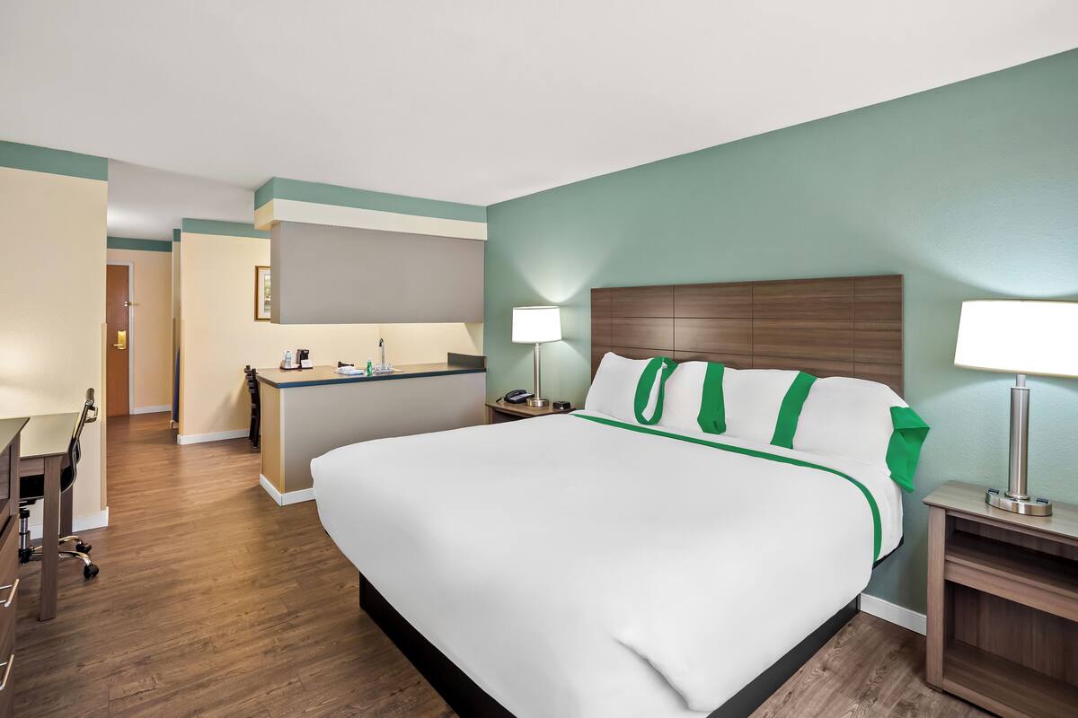 Quarto de hotel com uma cama grande, uma escrivaninha e uma cozinha compacta.