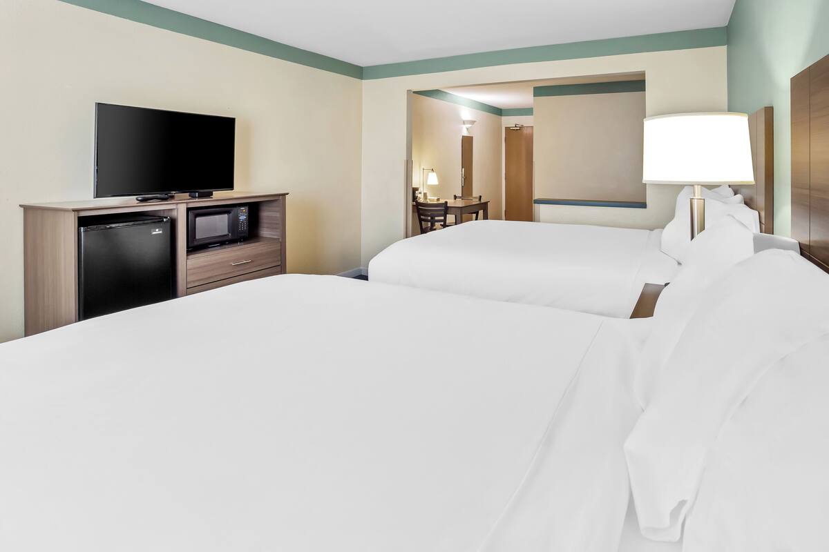 Quarto de hotel com duas camas, televisão, micro-ondas e secretária com luminária.