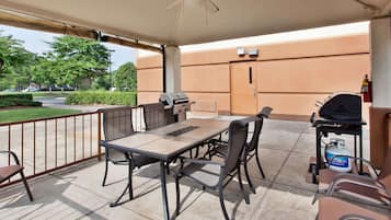 Um pátio externo com mesa, cadeiras, churrasqueira e ventoinha no teto.
