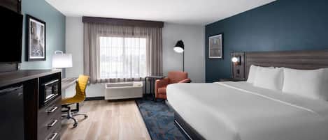 Quarto de hotel com uma cama grande, uma escrivaninha com cadeira, televisão e janela com cortinas.