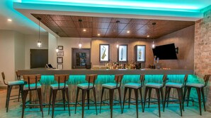 Uma área de bar com balcão, vários bancos altos e quadros nas paredes.
