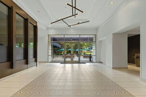 Um hall amplo com design moderno, destacando uma grande entrada em vidro, piso estampado e teto com vigas aparentes e luminárias.