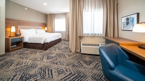 Quarto de hotel com uma cama grande, uma escrivaninha, uma cadeira, uma mesa de cabeceira e um ar condicionado fixado na parede.