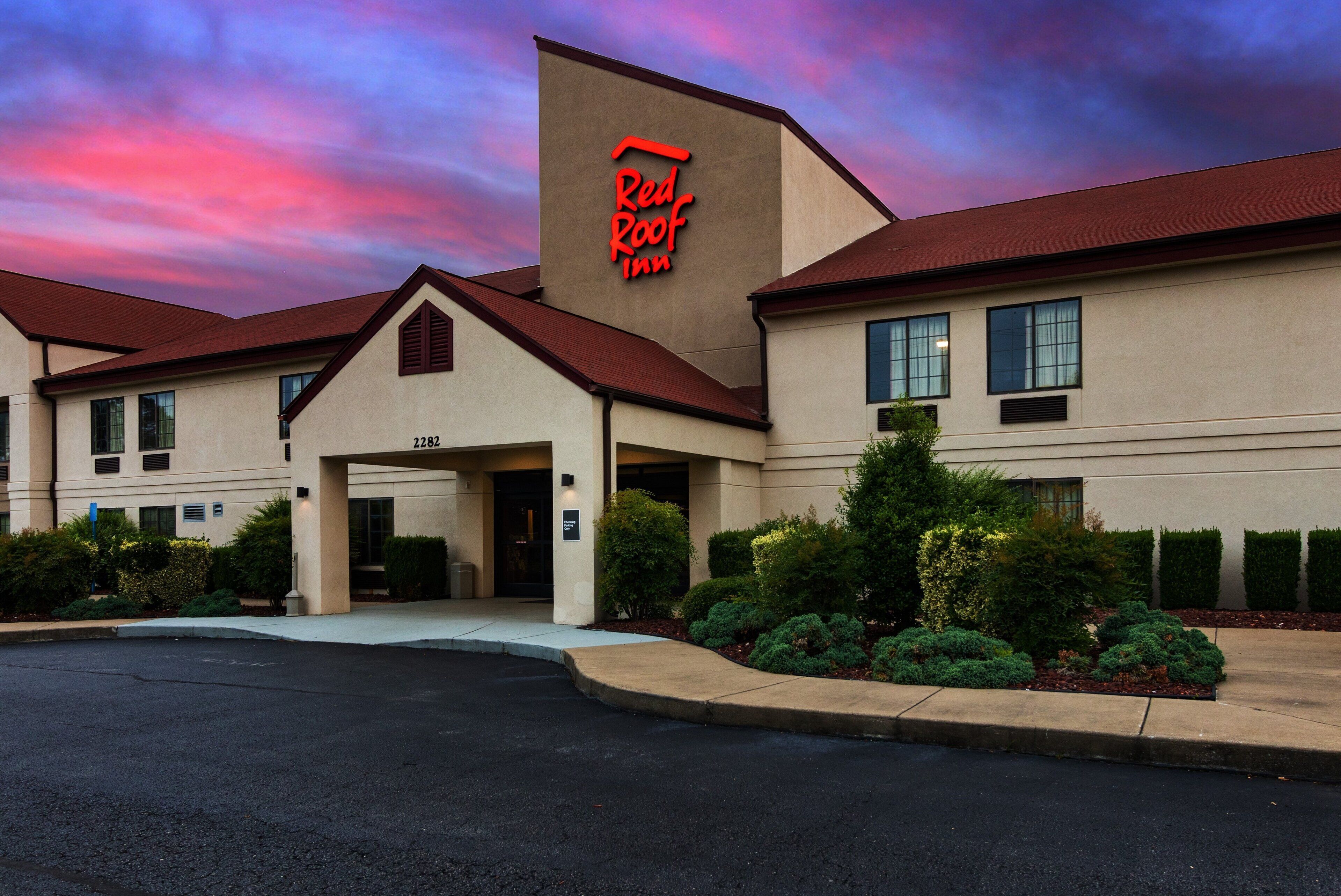 Um Red Roof Inn com design arquitetônico moderno, apresentando uma placa vermelha chamativa, estacionamento e paisagismo bem cuidado.
