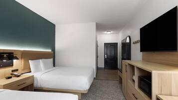 Quarto de hotel com duas camas, televisão, secretária com abajur e guarda-roupa.