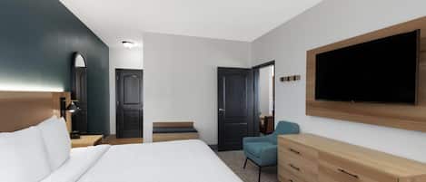 Quarto de hotel com uma cama grande, televisão fixada na parede, escrivaninha e uma cadeira.