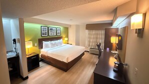 Quarto de hotel com uma cama, mesas de cabeceira, escrivaninha com luminária, telefone e quadros na parede.